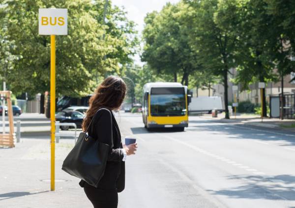 woman with coffee as bus approaches - Transportation Riders United
